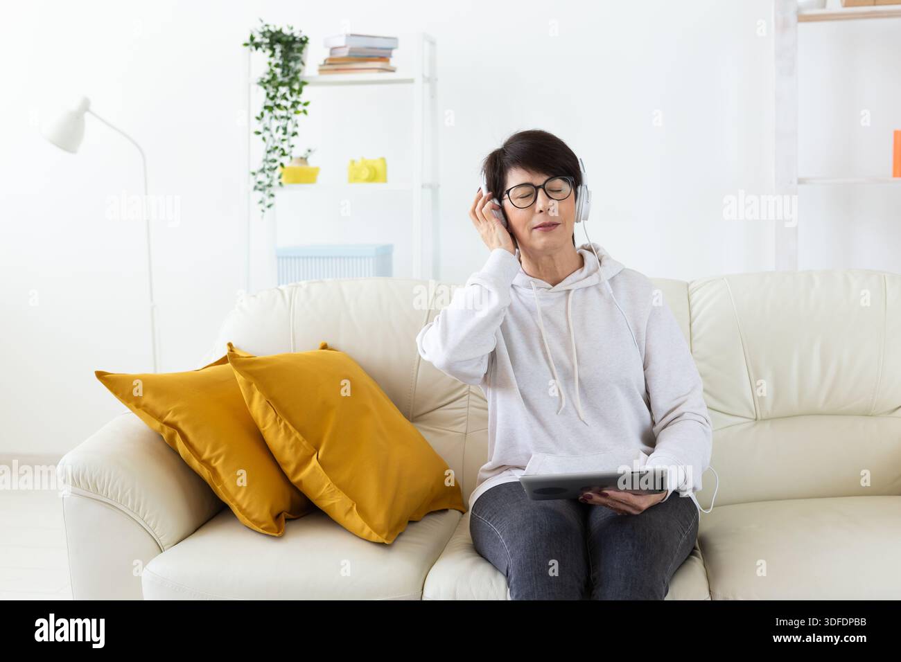 Woman listening to music with headphones on sofa in modern living room ...