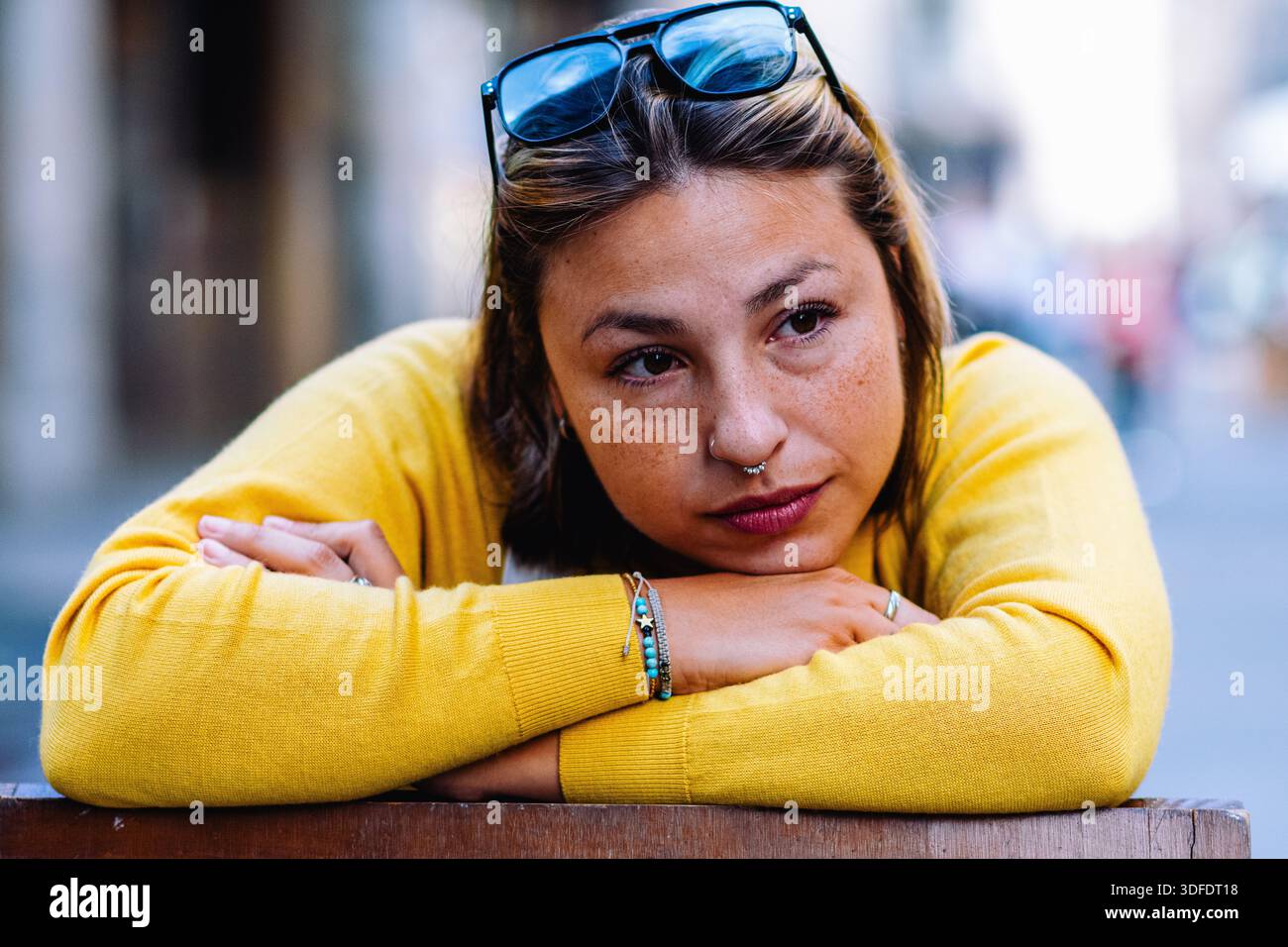 Young woman posing outdoors, casually leaning on a wooden surface with ...