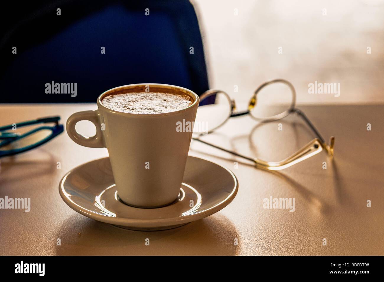 Warm coffee cup on a saucer resting on a white table next to reading ...