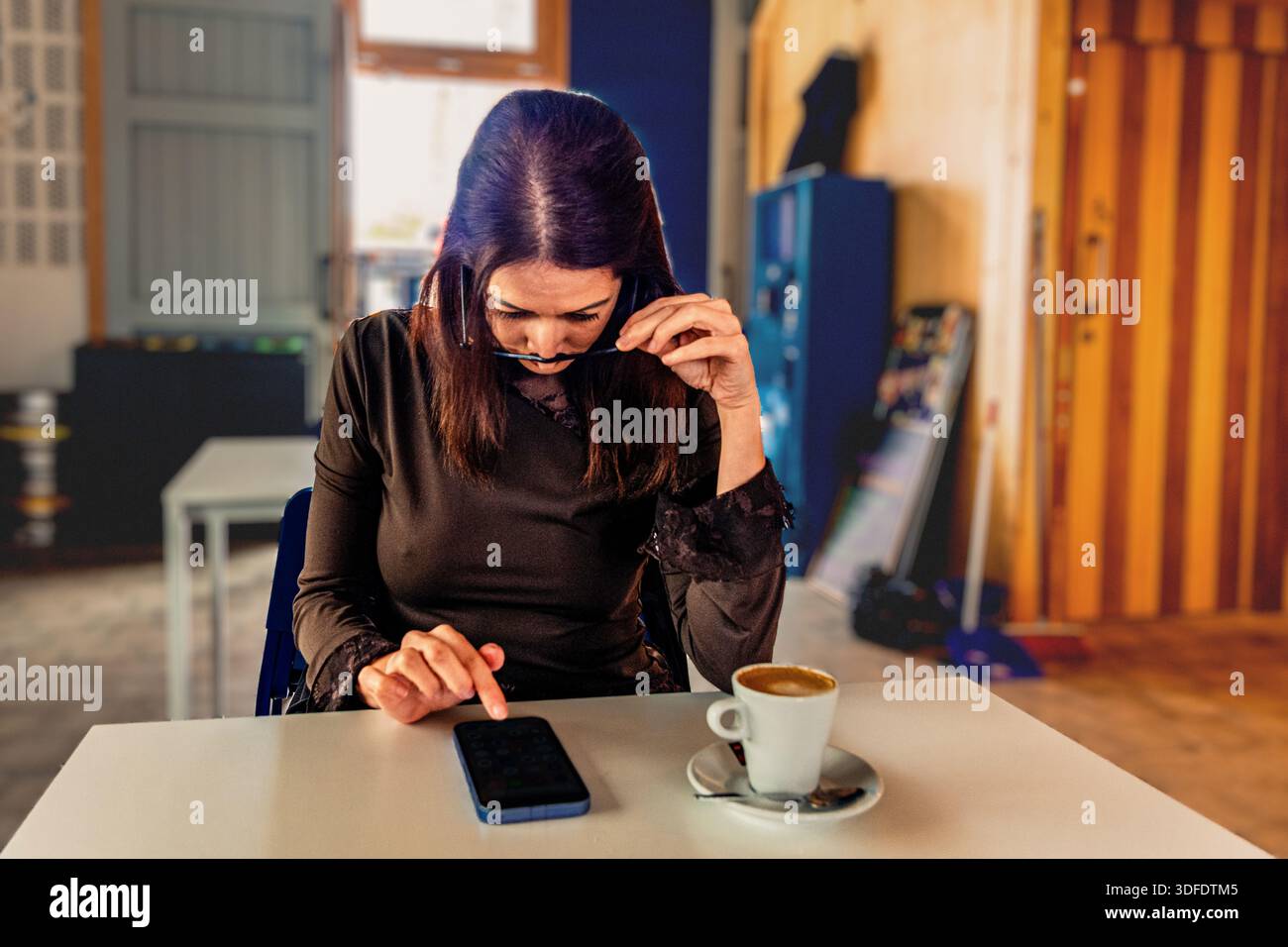 Woman holding glasses, looking down at a mobile phone, and touching the ...