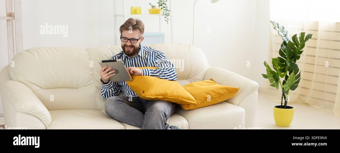 Man using tablet while sitting with pillows on sofa in bright living ...