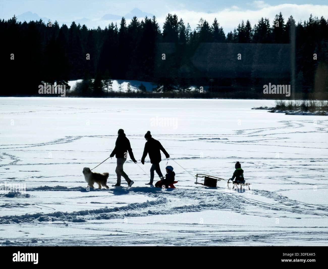 People walk across the snow-covered frozen lake Elbsee under a clear ...