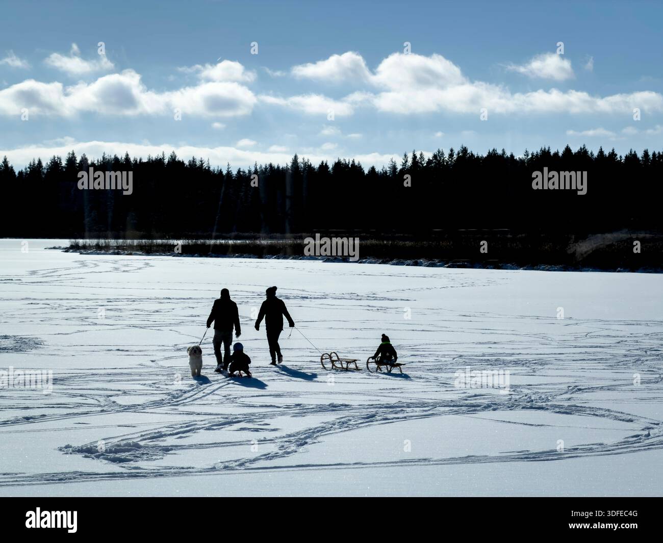 People walk across the snow-covered frozen lake Elbsee under a clear ...