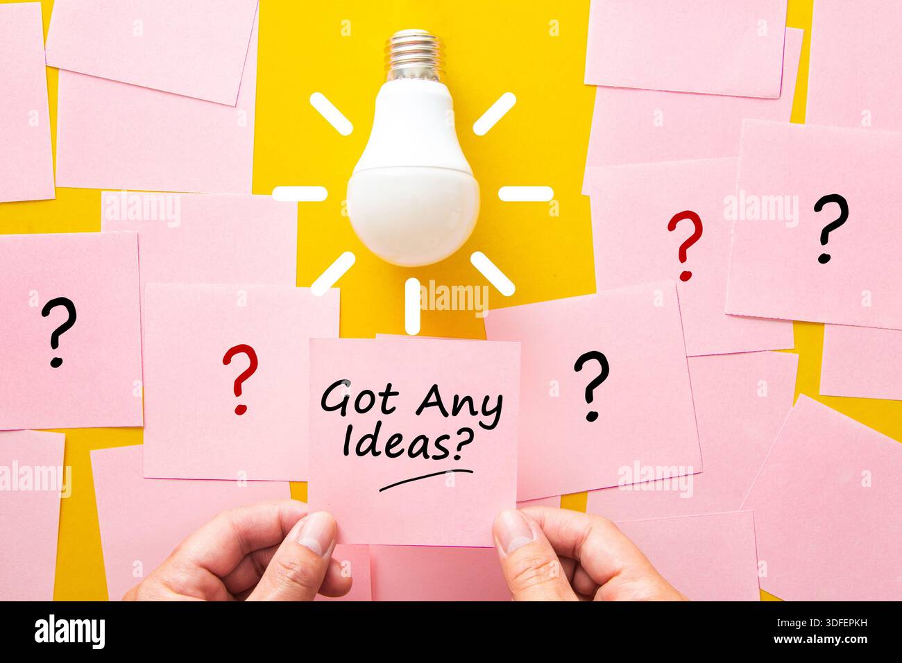 Light bulb shining above pink sticky notes with question marks and text ...