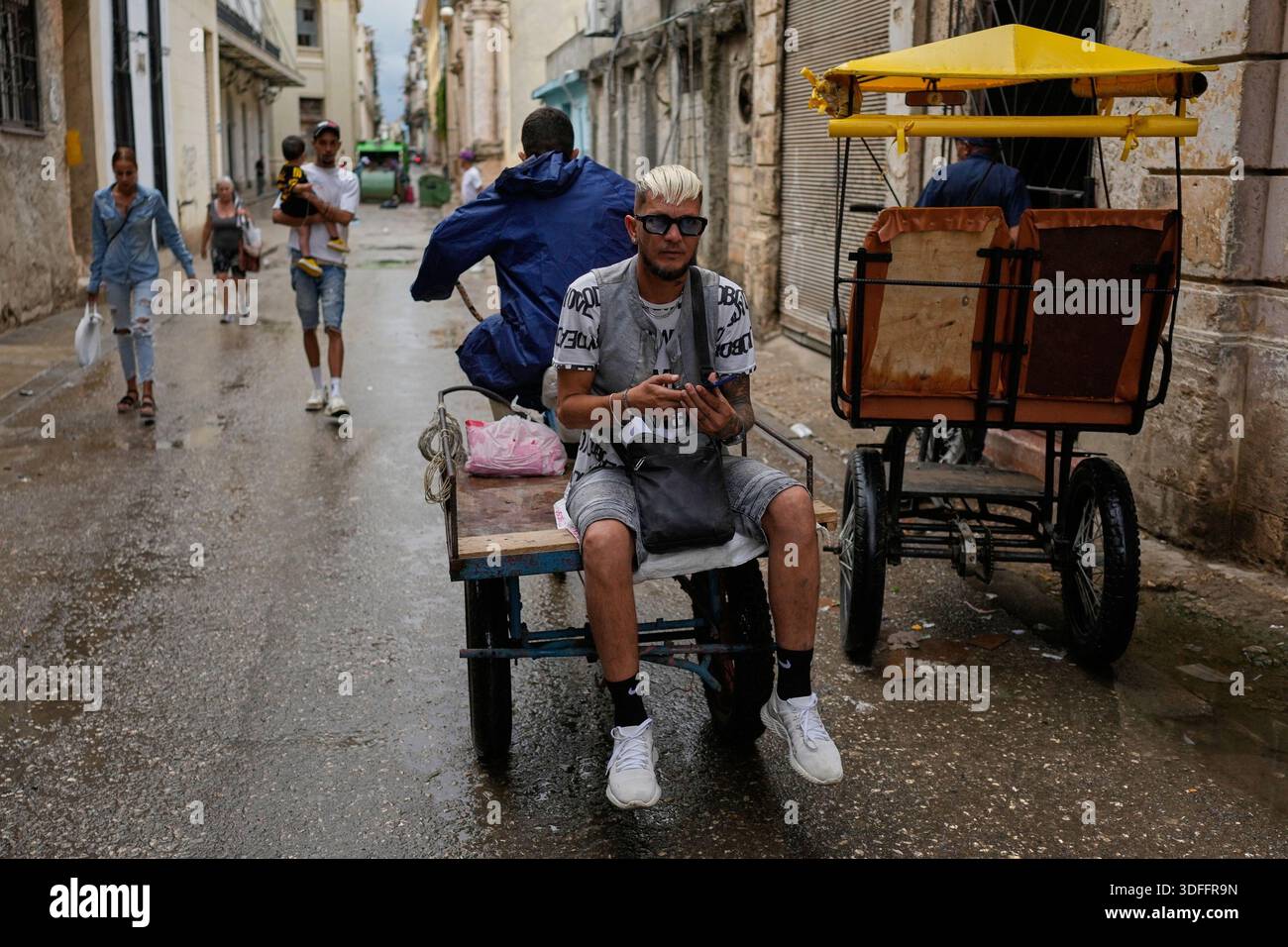 A man holds his cell phone as he rides on the back of a bicycle cart in ...