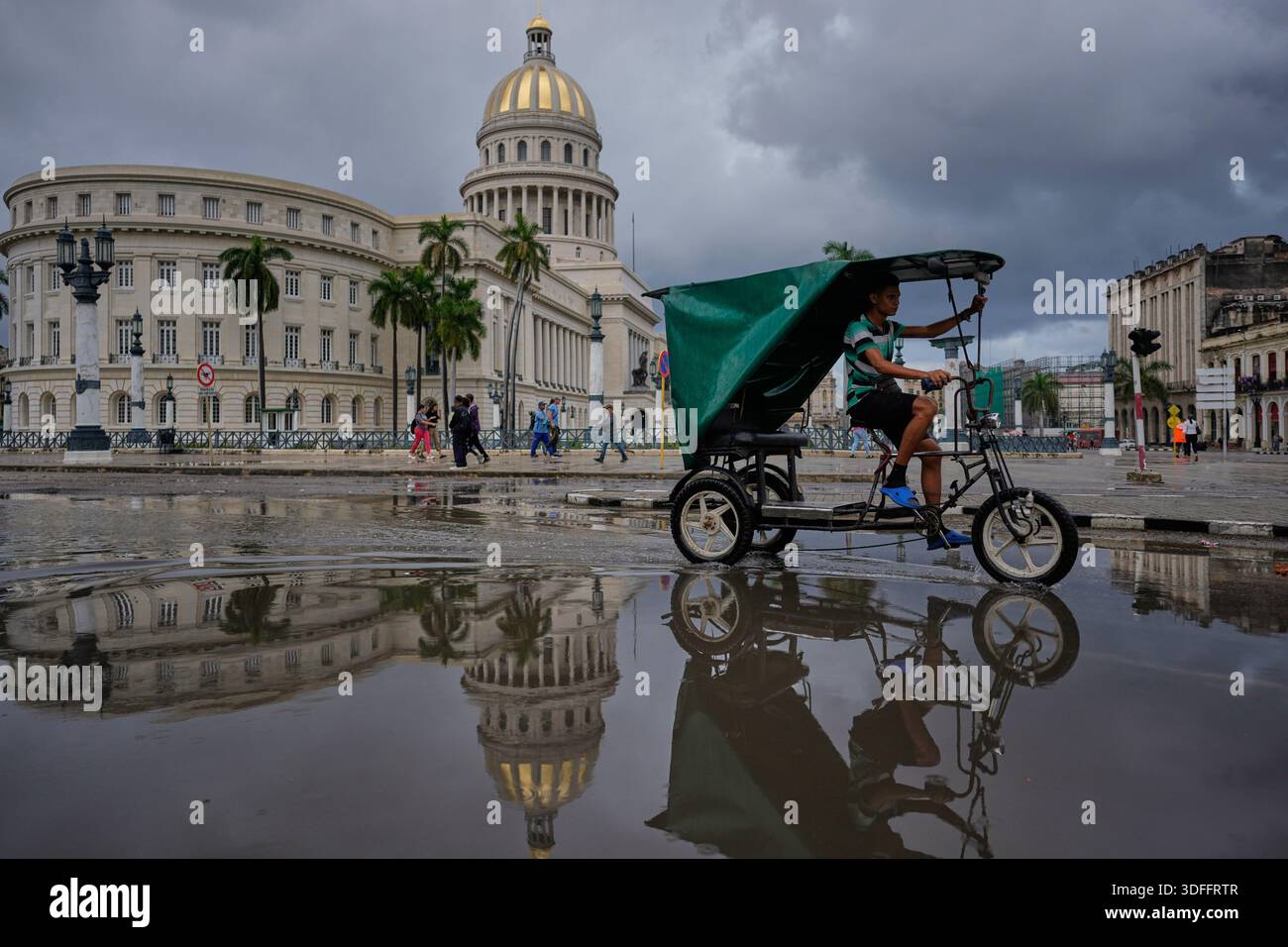 A bicycle taxi driver crosses a puddle reflecting the Capitolio, the ...
