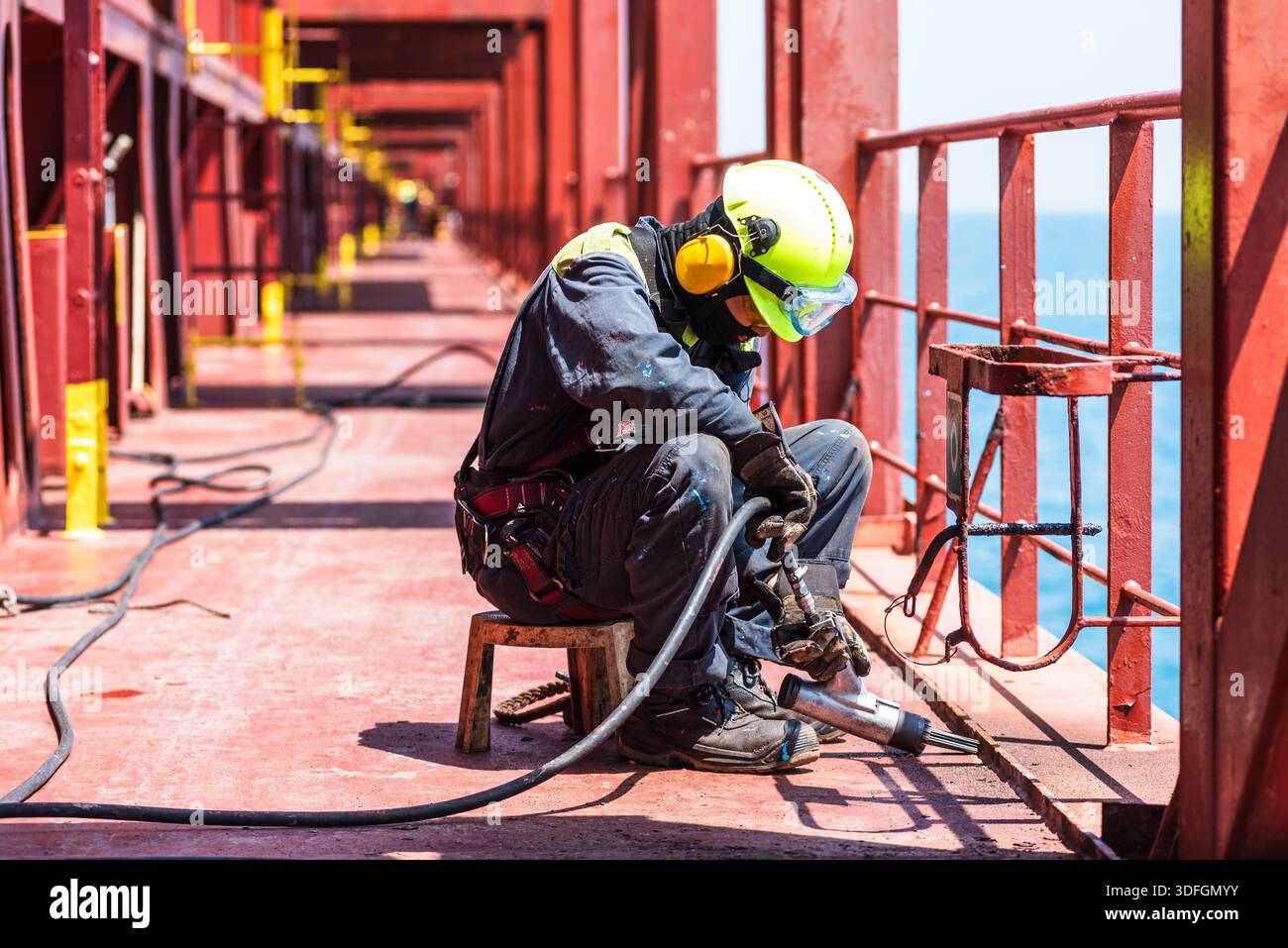 Seafarer wearing PPE removes rust from a ship deck using a pneumatic ...