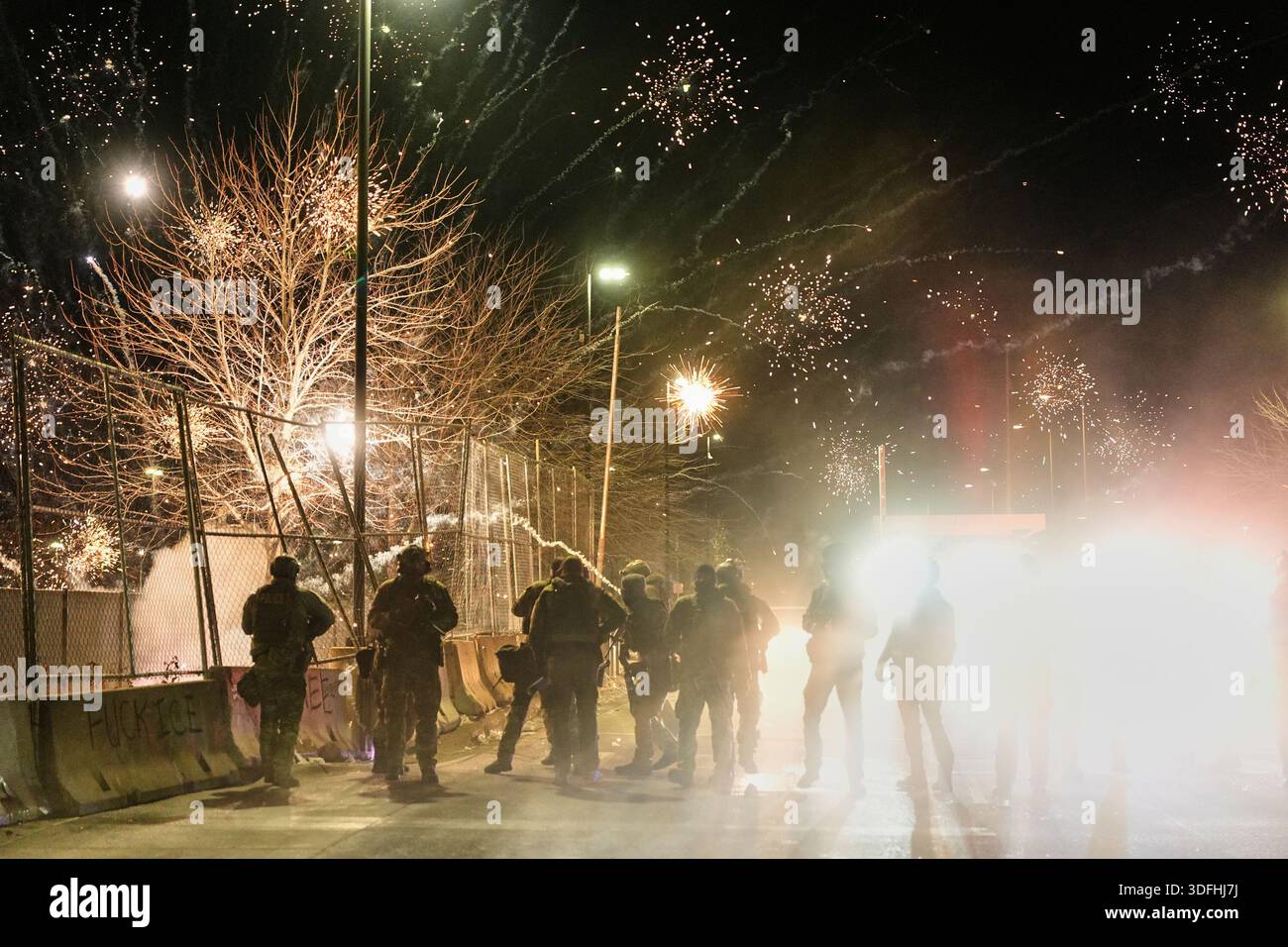 Federal immigration officers look on as fireworks set off by protesters ...