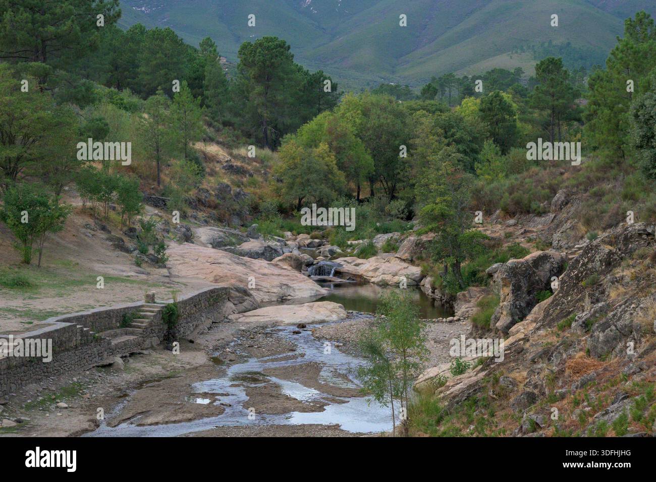 Empty natural river pool surrounded by rocks trees and green hills in ...