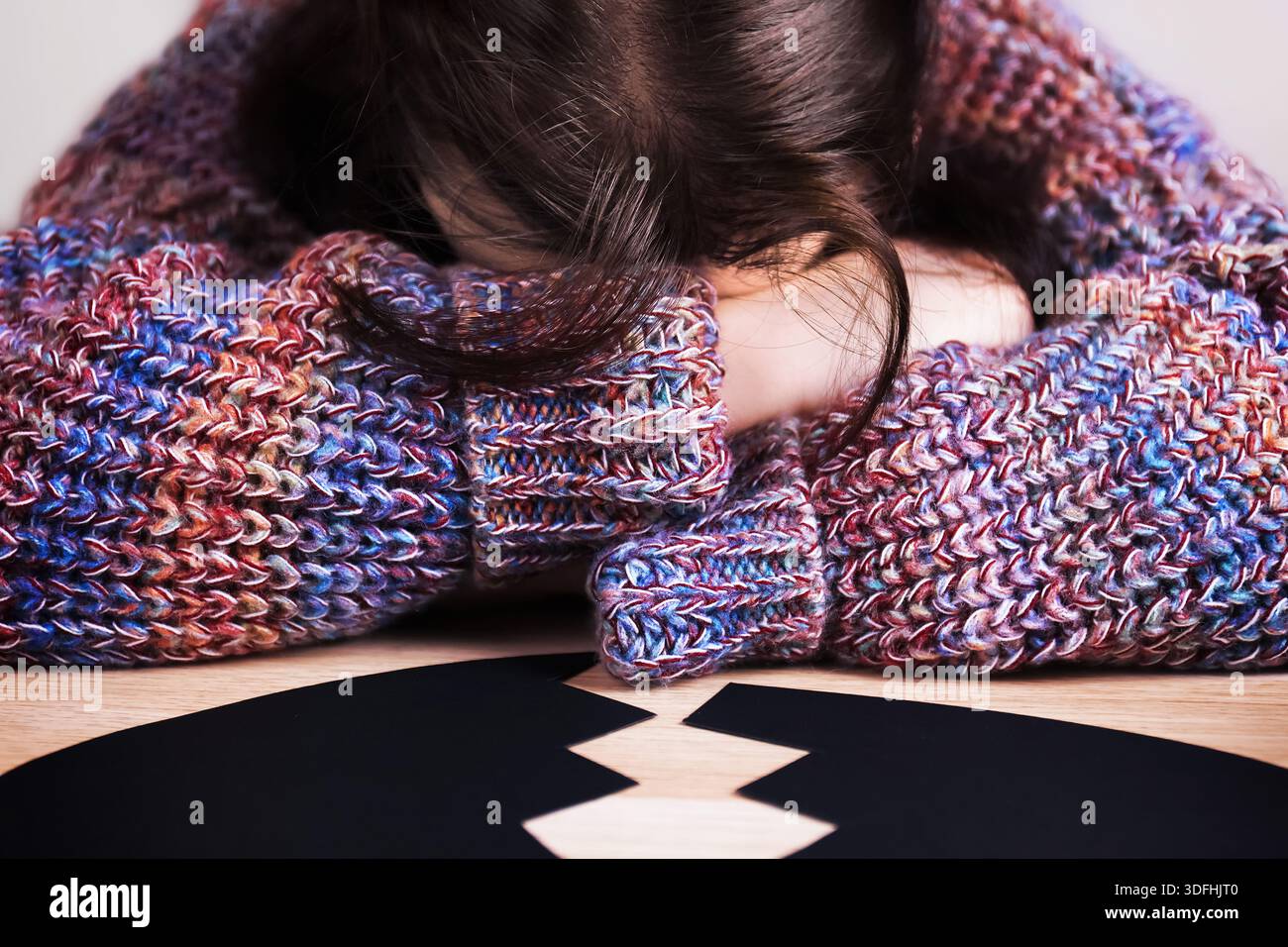 Depressed woman hiding face in arms near a broken black heart. Sad ...