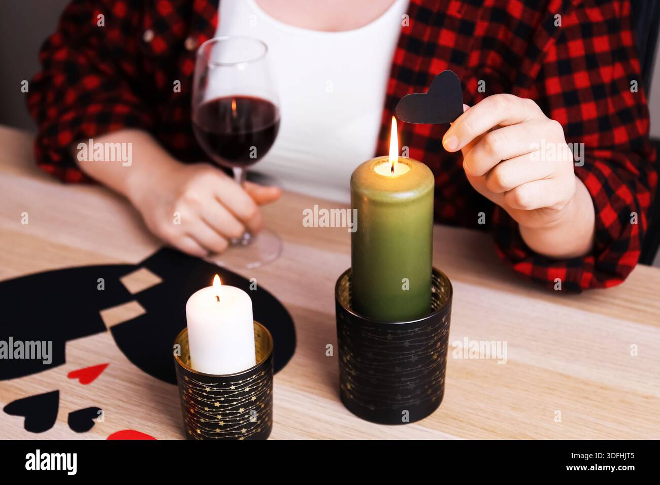 Woman burning a black paper heart over a candle flame while holding ...