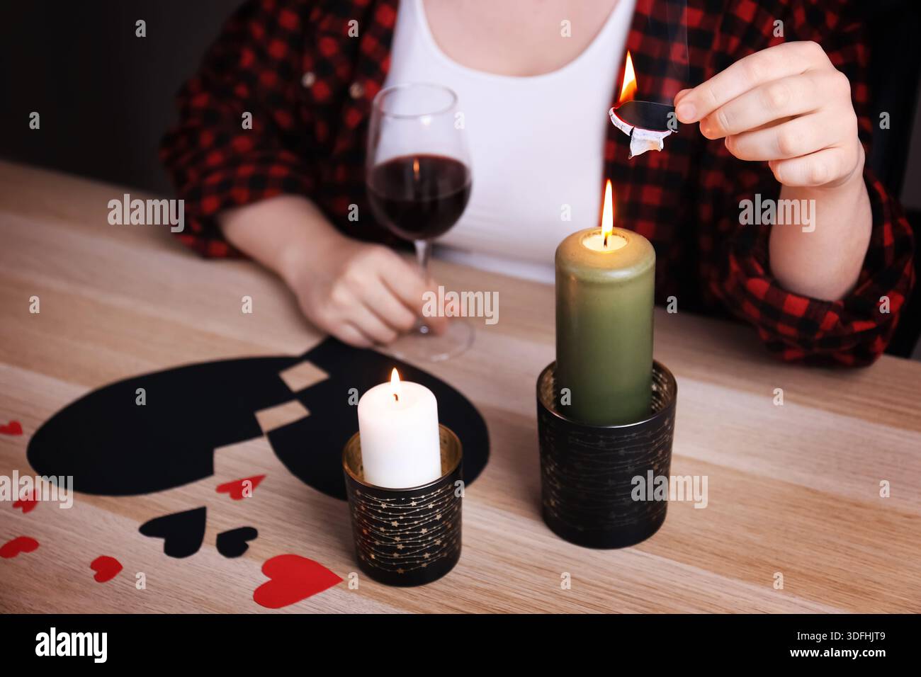 Woman burning a photo over a candle flame. Broken black heart and wine ...