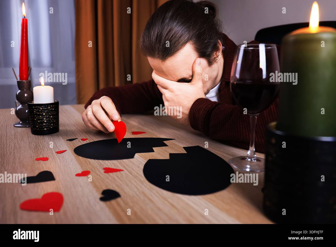 Crying man with face in hand sitting at table with wine and broken ...