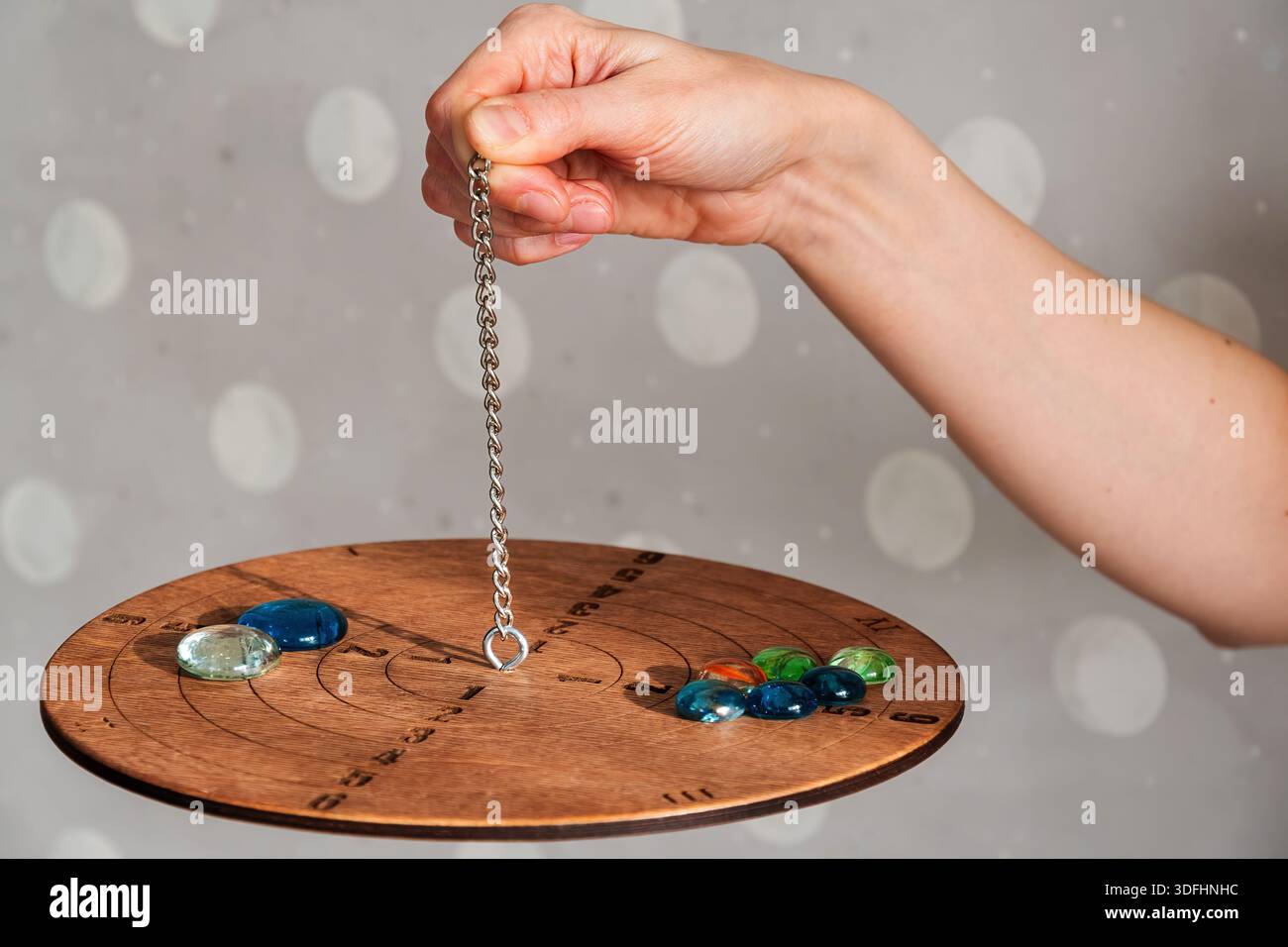 Female hand holds a pendulum over a wooden balance board game with ...