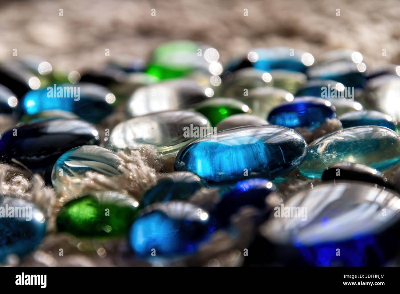 Close-up of vibrant blue and green glass pebbles on a soft, textured ...