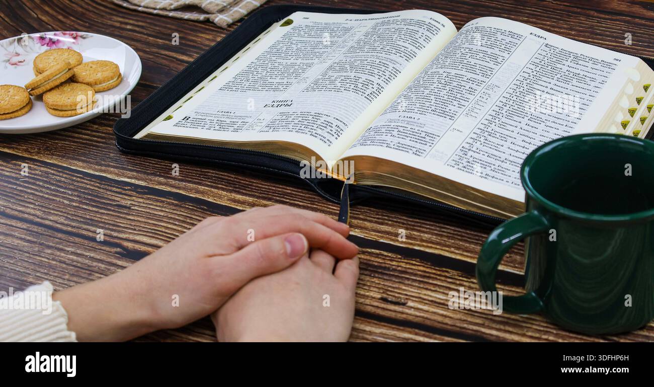 Hands of a girl praying in front of an open Bible on a wooden table ...