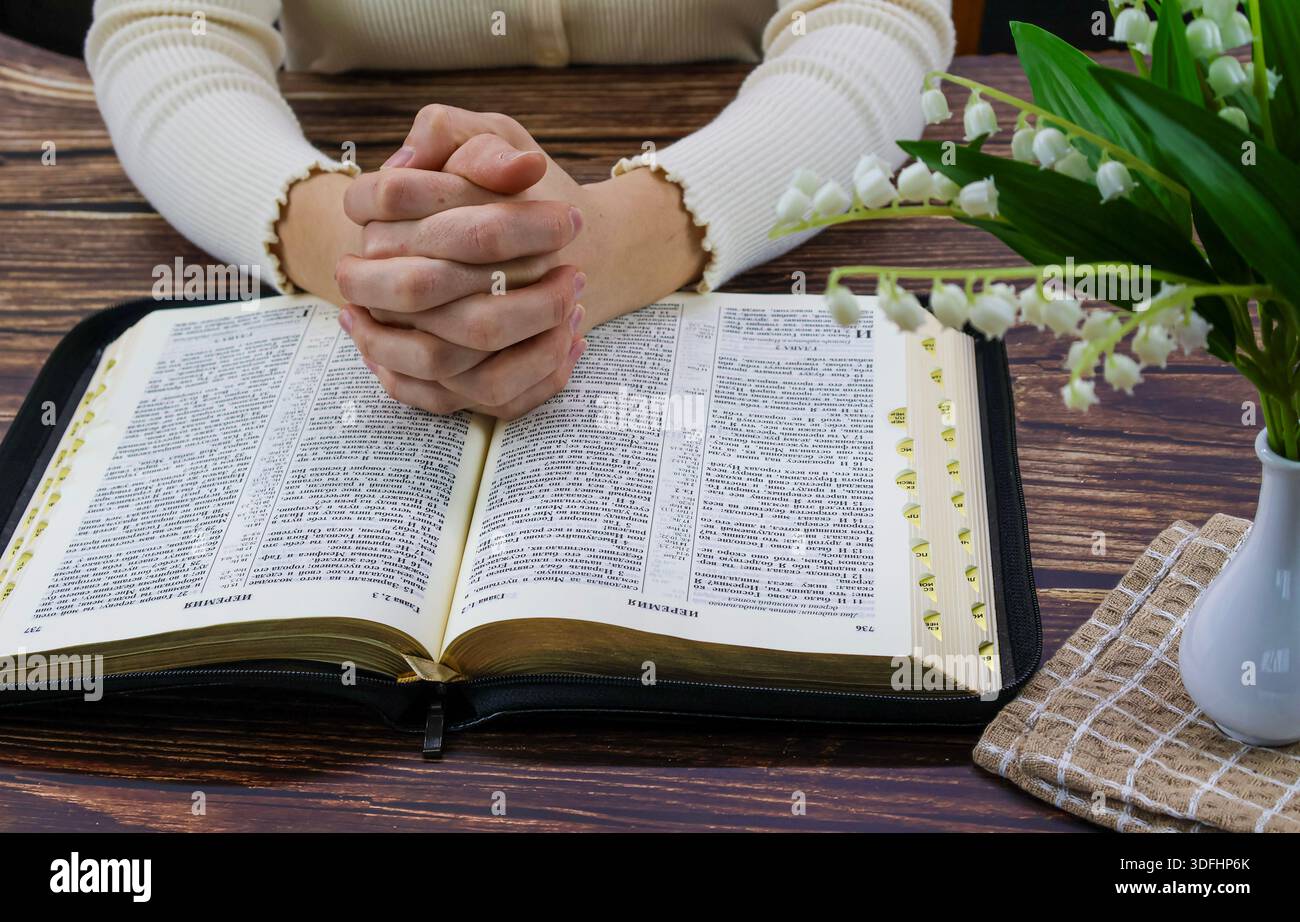 Hands of a girl praying in front of an open Bible on a wooden table ...