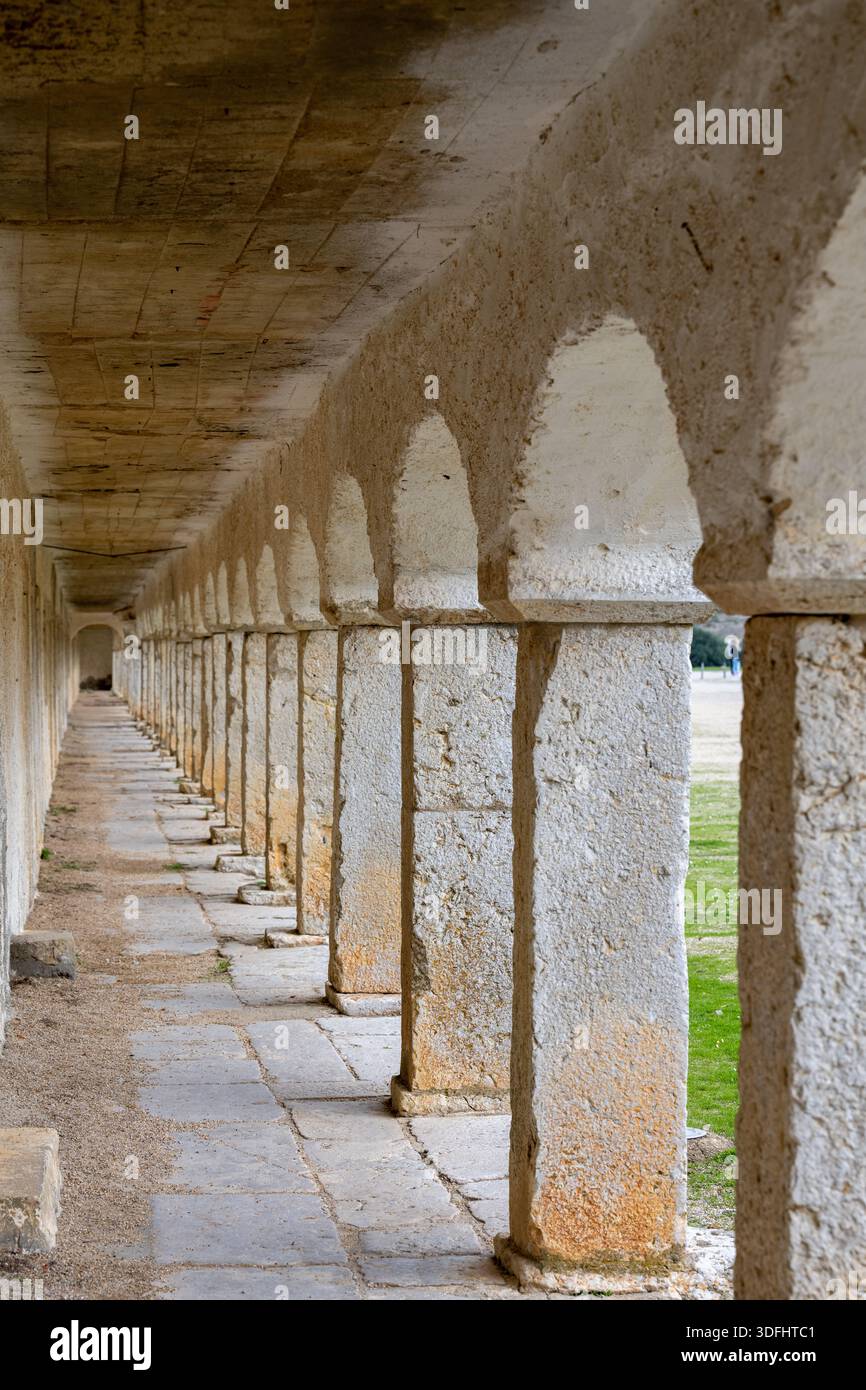 A covered stone colonnade with repeating arches stretches through the ...