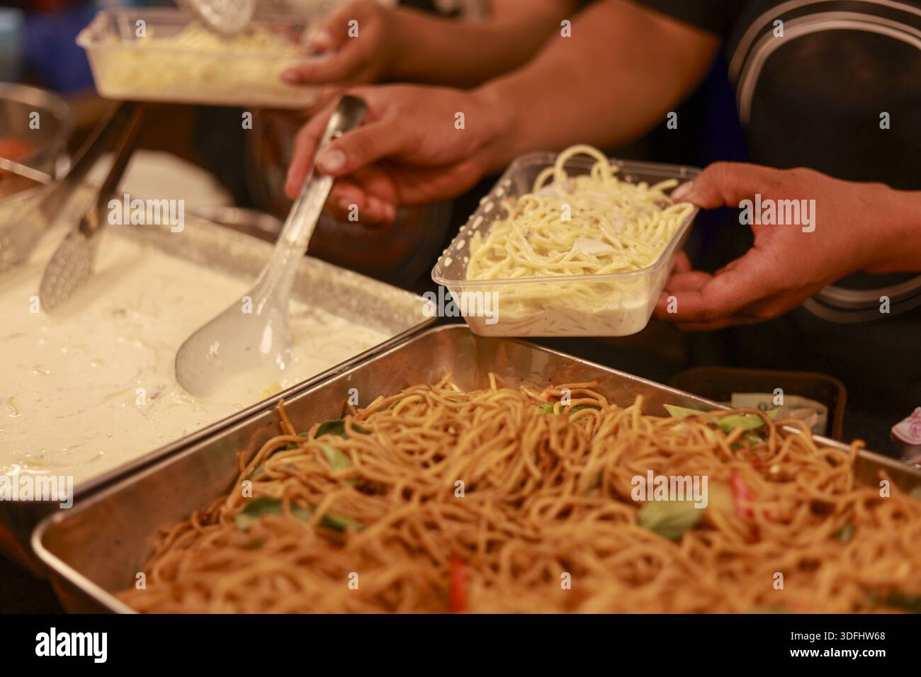 Close up hands serving street food spaghetti pasta white sauce into ...
