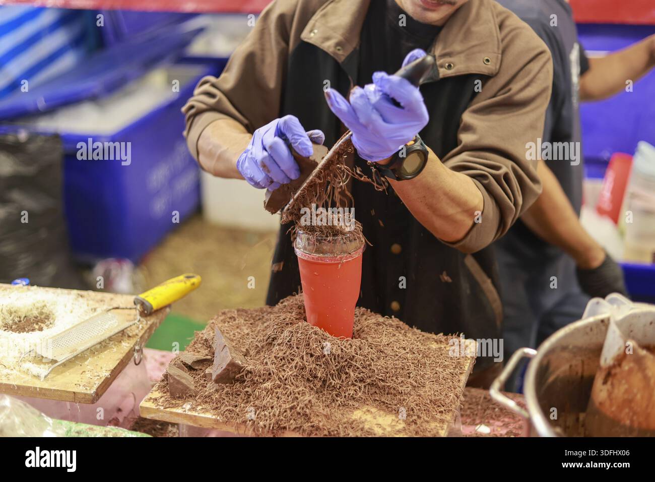 Focused vendor carefully shaving sweet cocoa chocolate powder into cold ...