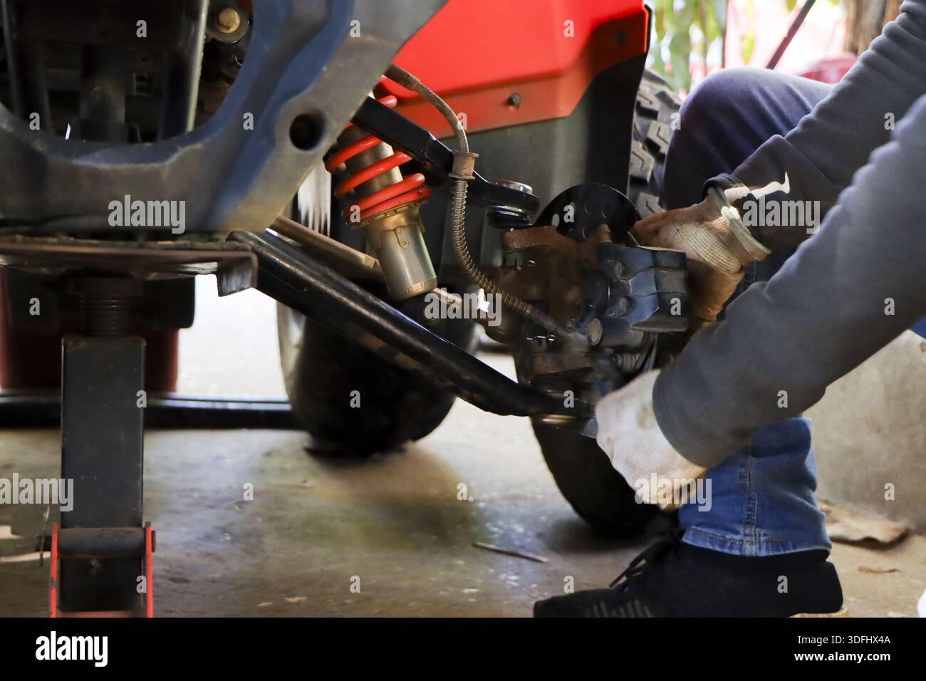 Mechanic performing maintenance on vehicle suspension system with jack ...