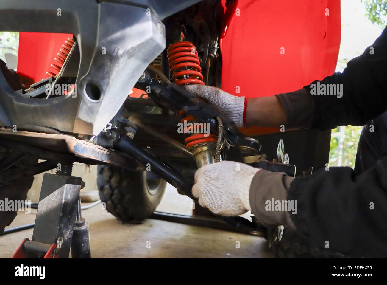 Concentrated mechanic hands wearing gloves repairing red shock absorber ...