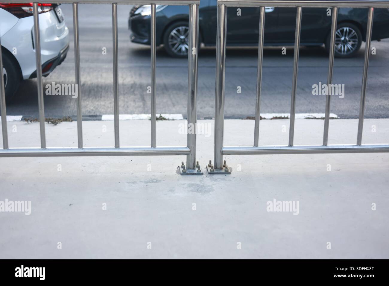 Shiny metal railing barrier fence stand on concrete footpath beside ...