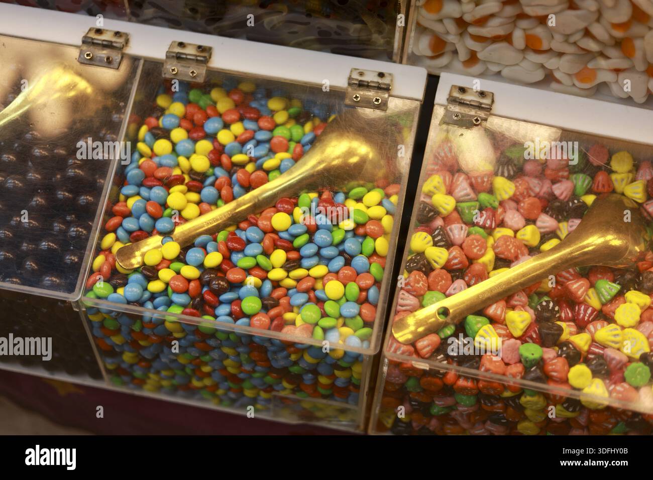 Colorful sweet candy in plastic container bin with golden scoop display ...