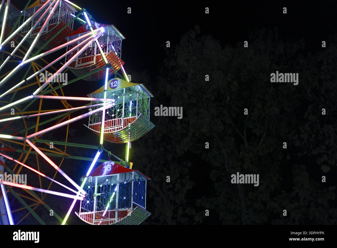 Colorful neon ferris wheel ride spinning against dark night sky showing ...