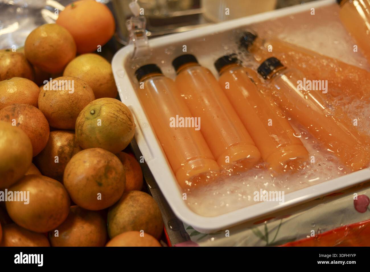 Refreshing cold orange juice in plastic bottle on ice tray next to pile ...
