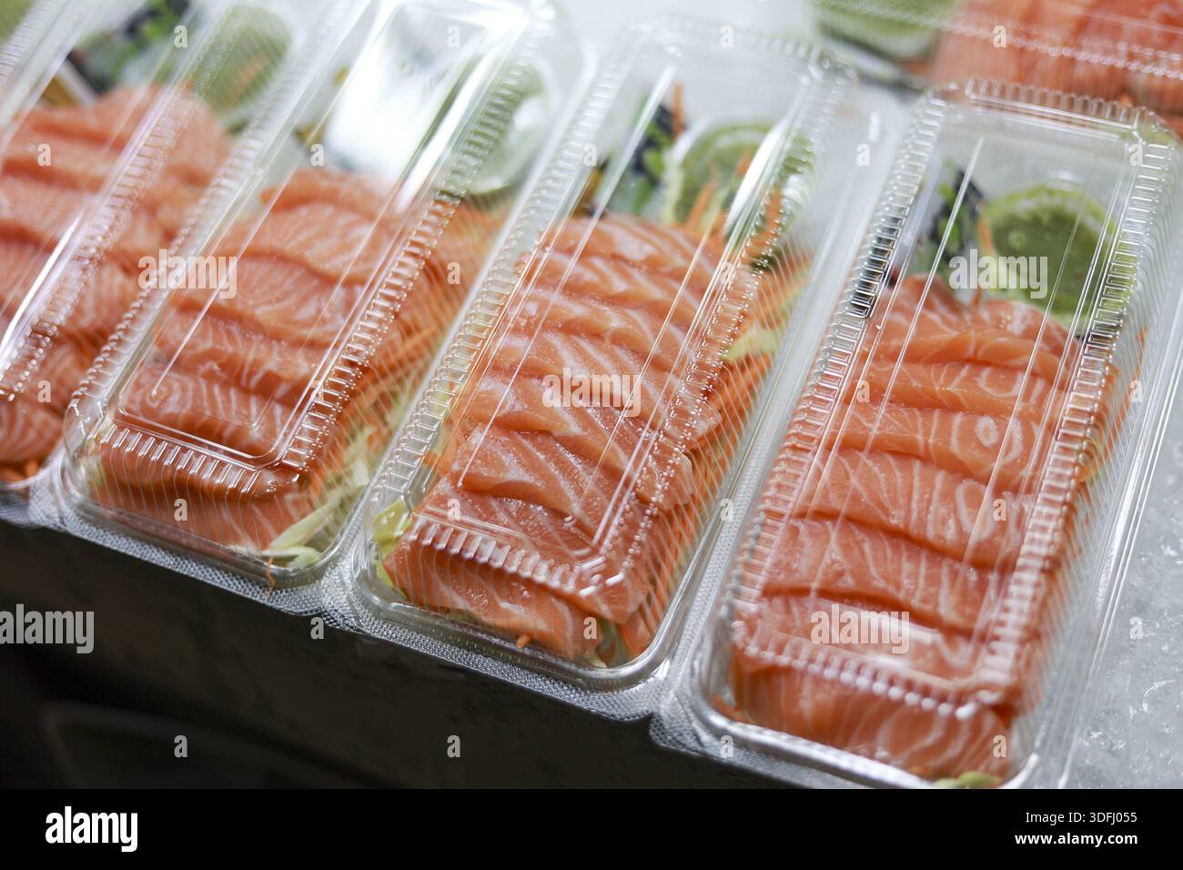 Fresh sliced salmon sashimi arranged neatly in clear plastic takeaway ...