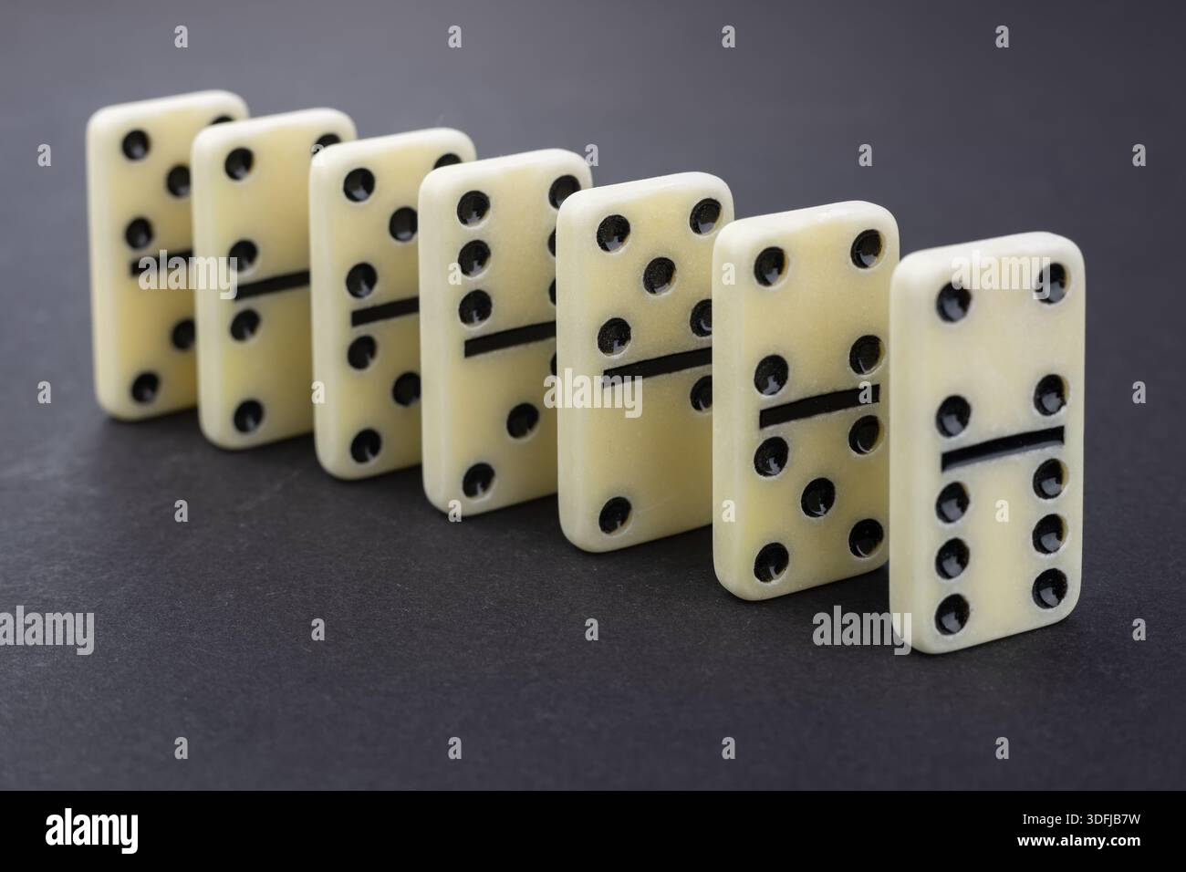 Domino tiles lined up in a perfect sequence on a dark green surface ...