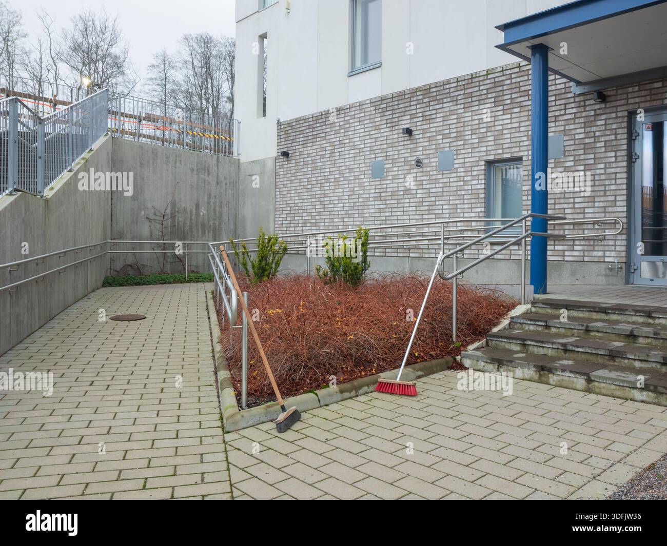 An outdoor building entrance area with a ramp, stair, and a brick wall ...