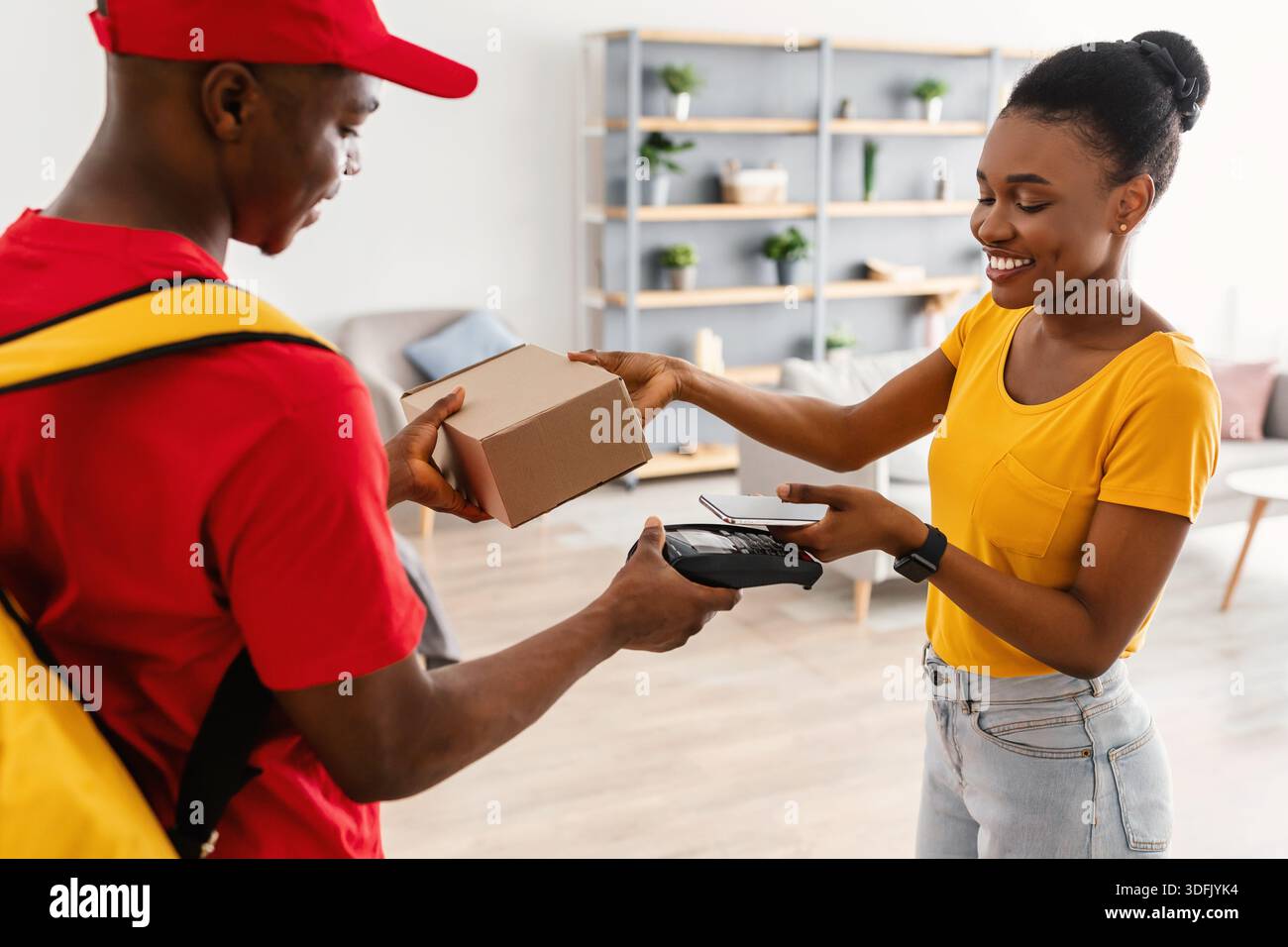 African Woman Receiving Box From Courier Paying With Smartphone Indoor ...
