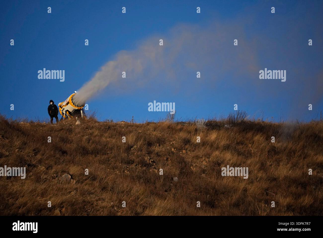 FILE - A person works at a snow making machine on a hill overlooking ...