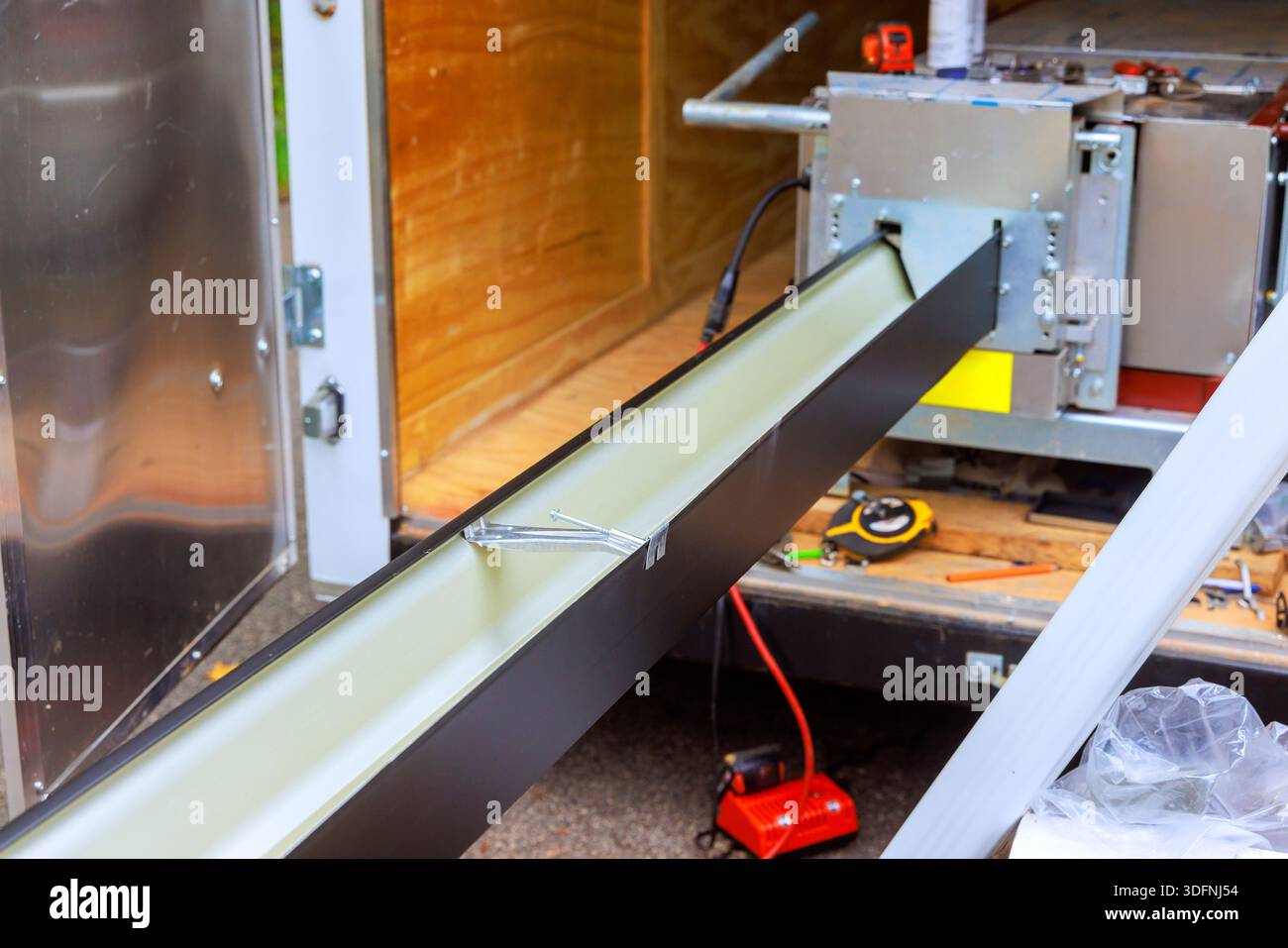 Workers assemble gutter channels inside trailer using various tools ...