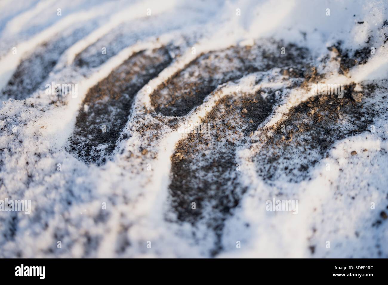 Macro view of snowy ground with dark tire track grooves and road grit ...