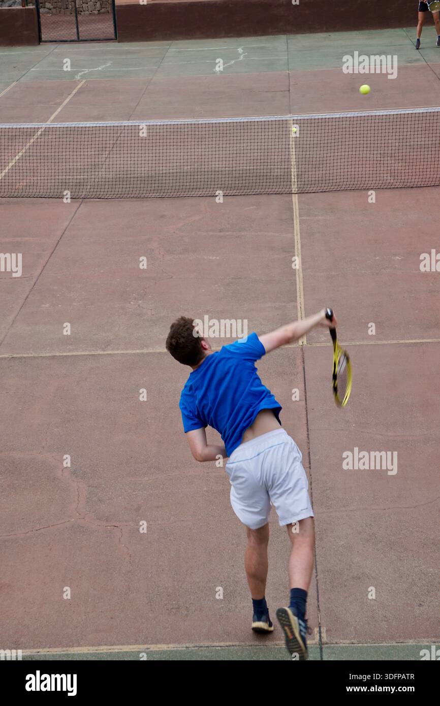 Male tennis player serving during an outdoor tennis match, captured mid ...