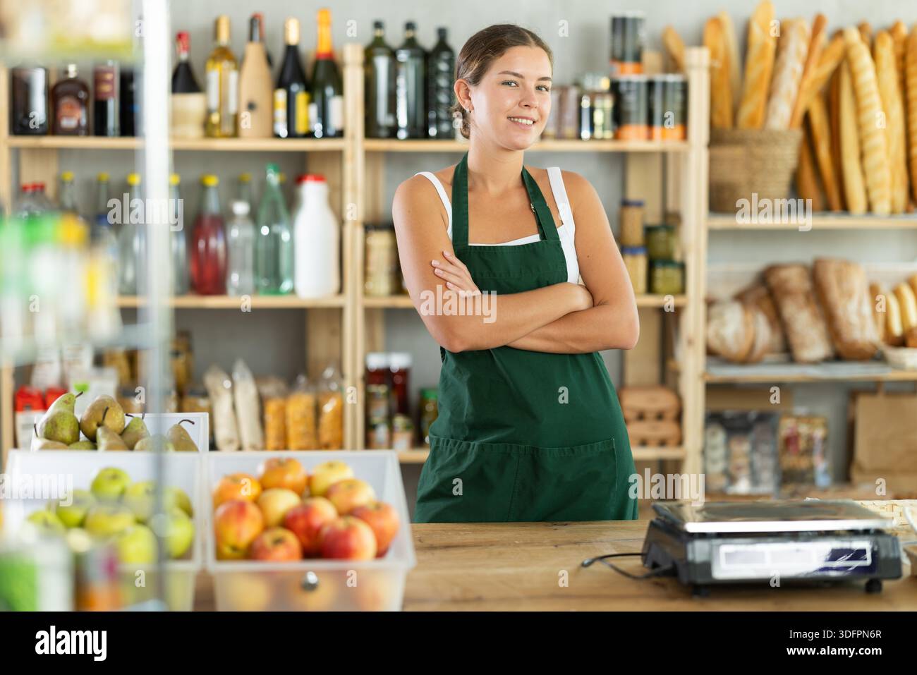 Portrait of smiling female salesperson in apron behind supermarket ...
