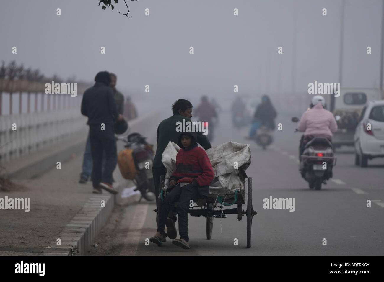 A ragpicker boy rides on the back of a bicycle cart through dense fog ...