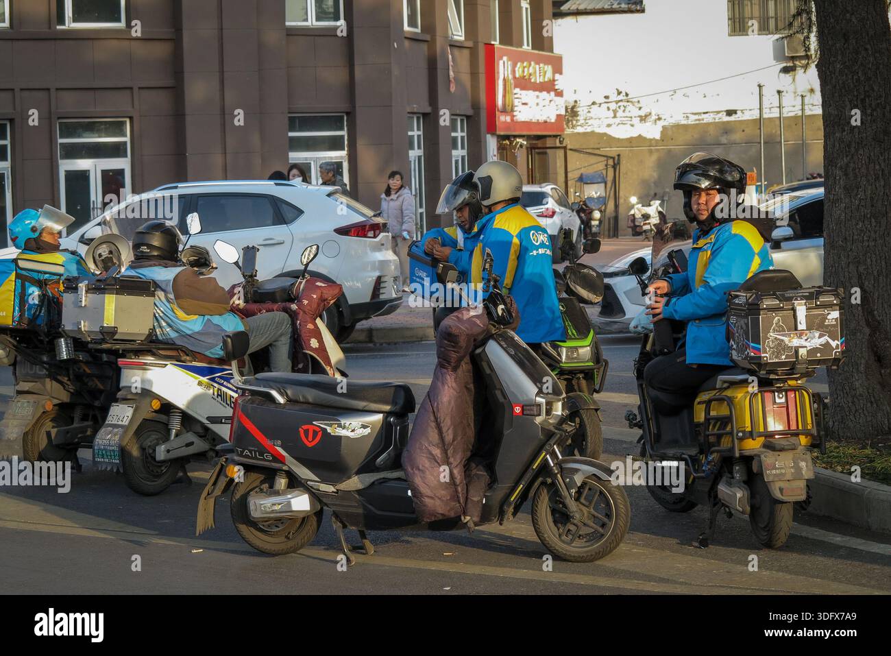 Delivery riders wait on their scooters at a street corner, with a ...