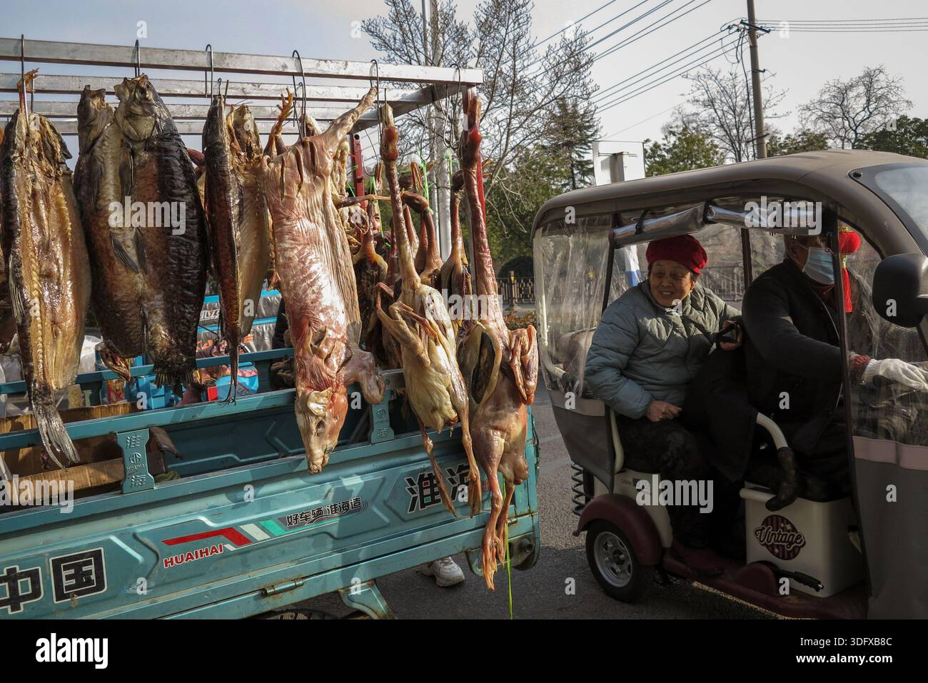 A three-wheeled vehicle is loaded with dried fish and poultry, and two ...