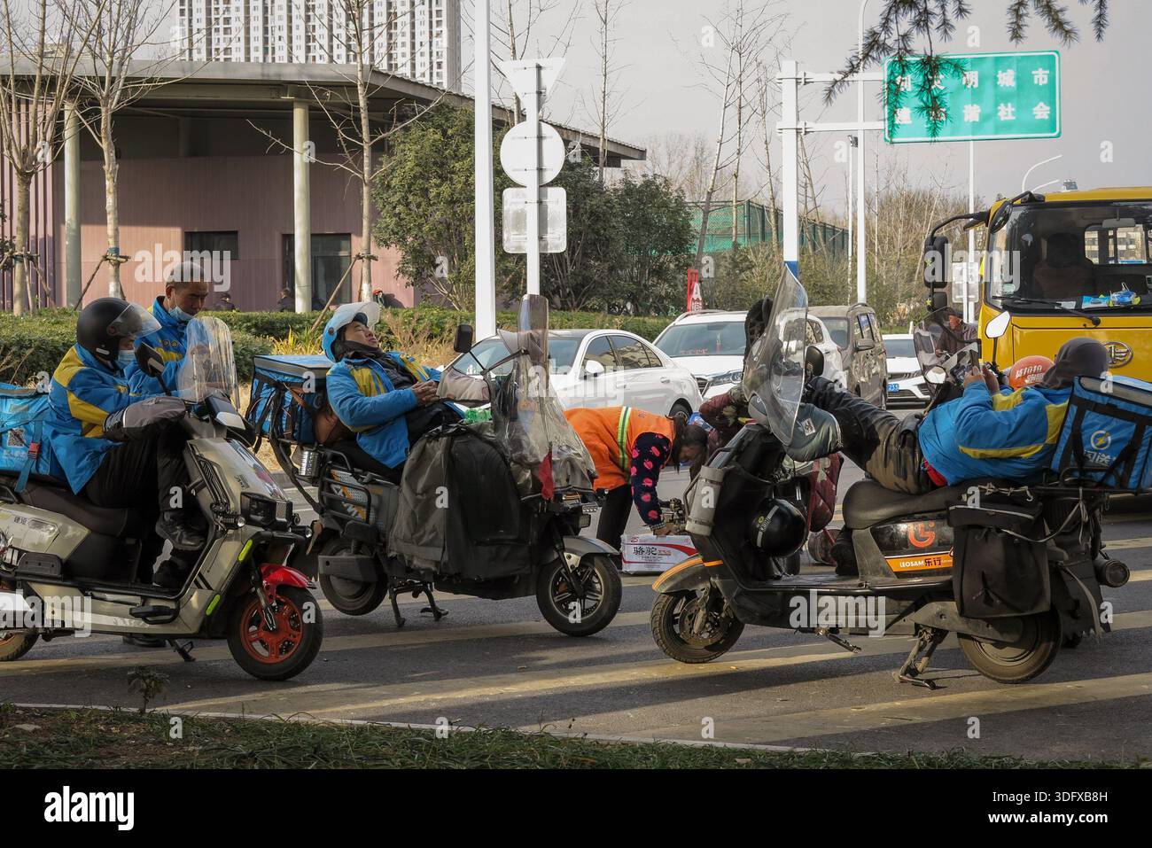Delivery riders in blue uniforms rest on their scooters by the roadside ...