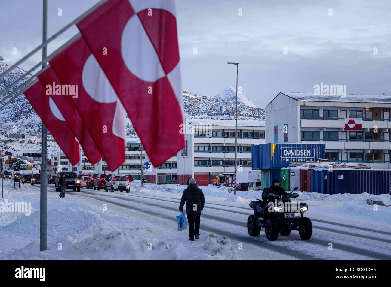 A man rides by on a quad bike past a row of Greenlandic national flags in Nuuk, Greenland ...
