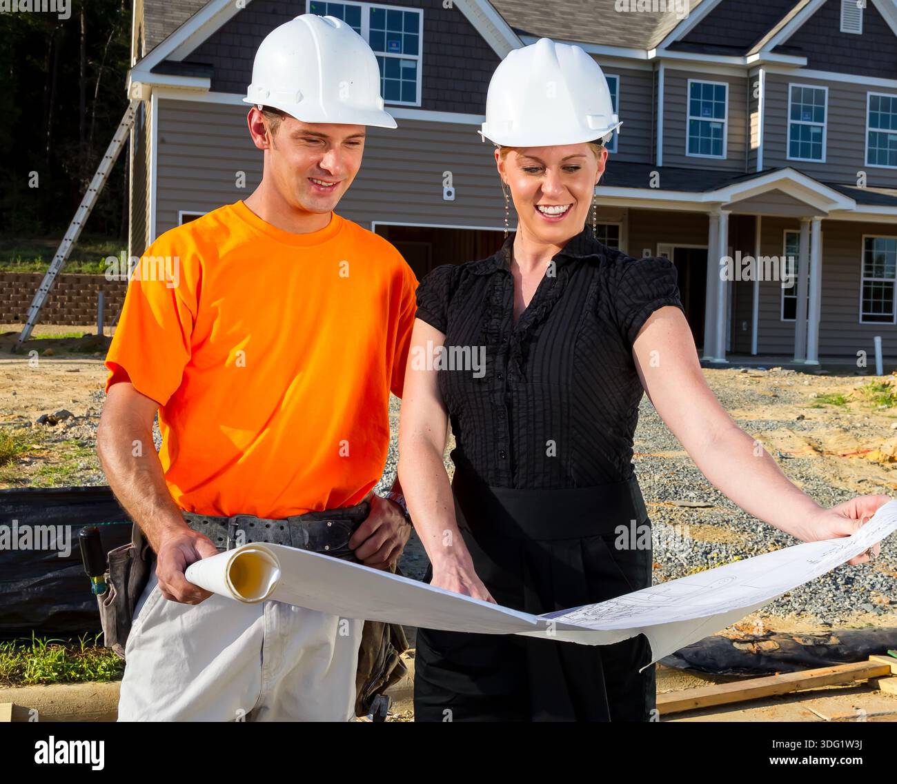 At a sunlit build site, a construction worker and an engineer study ...