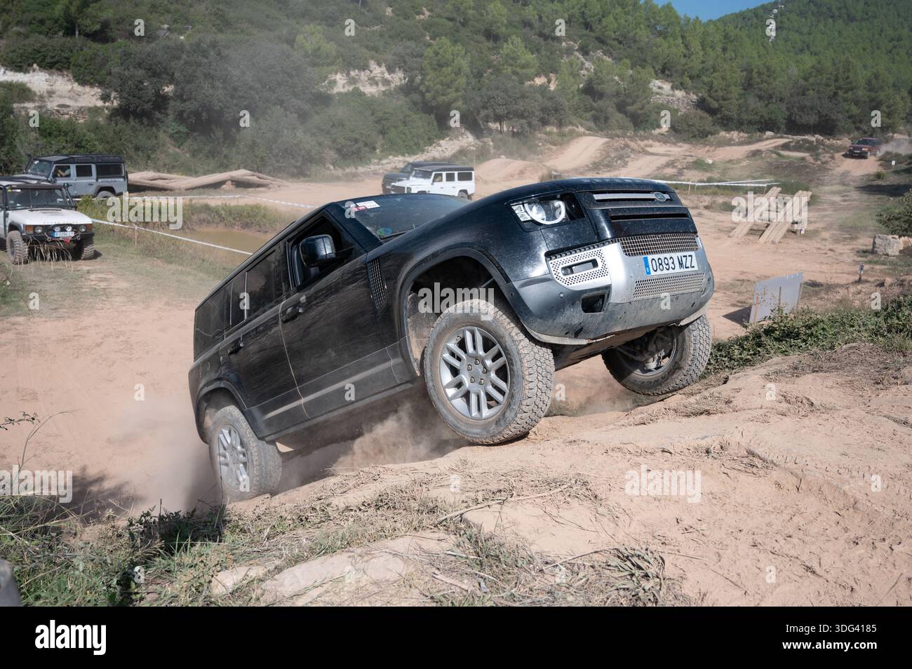 Modern black Land Rover Defender L663 tackling a steep, slippery dirt ...