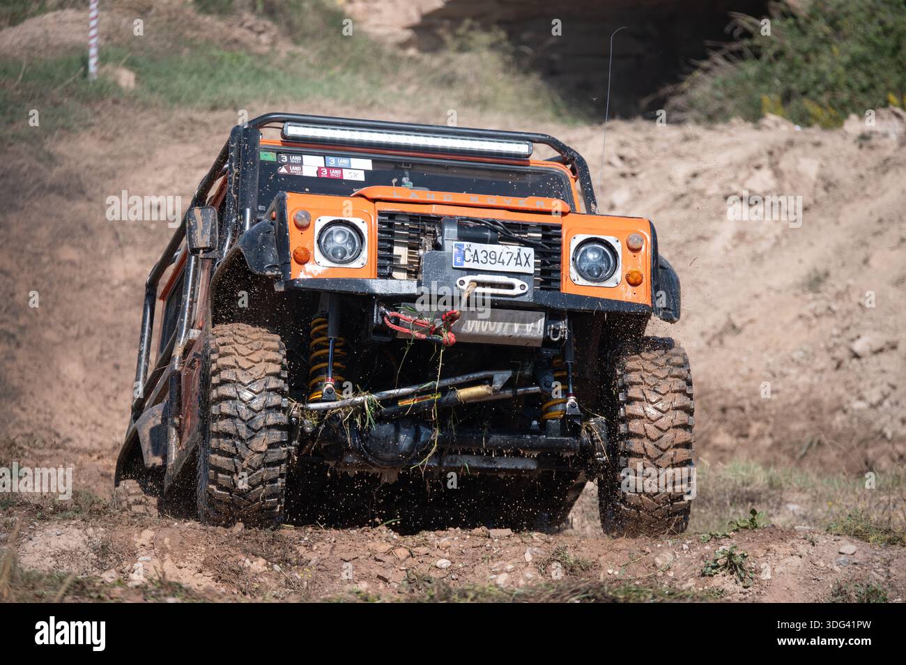 Front view of a modified orange Land Rover Defender climbing a steep ...