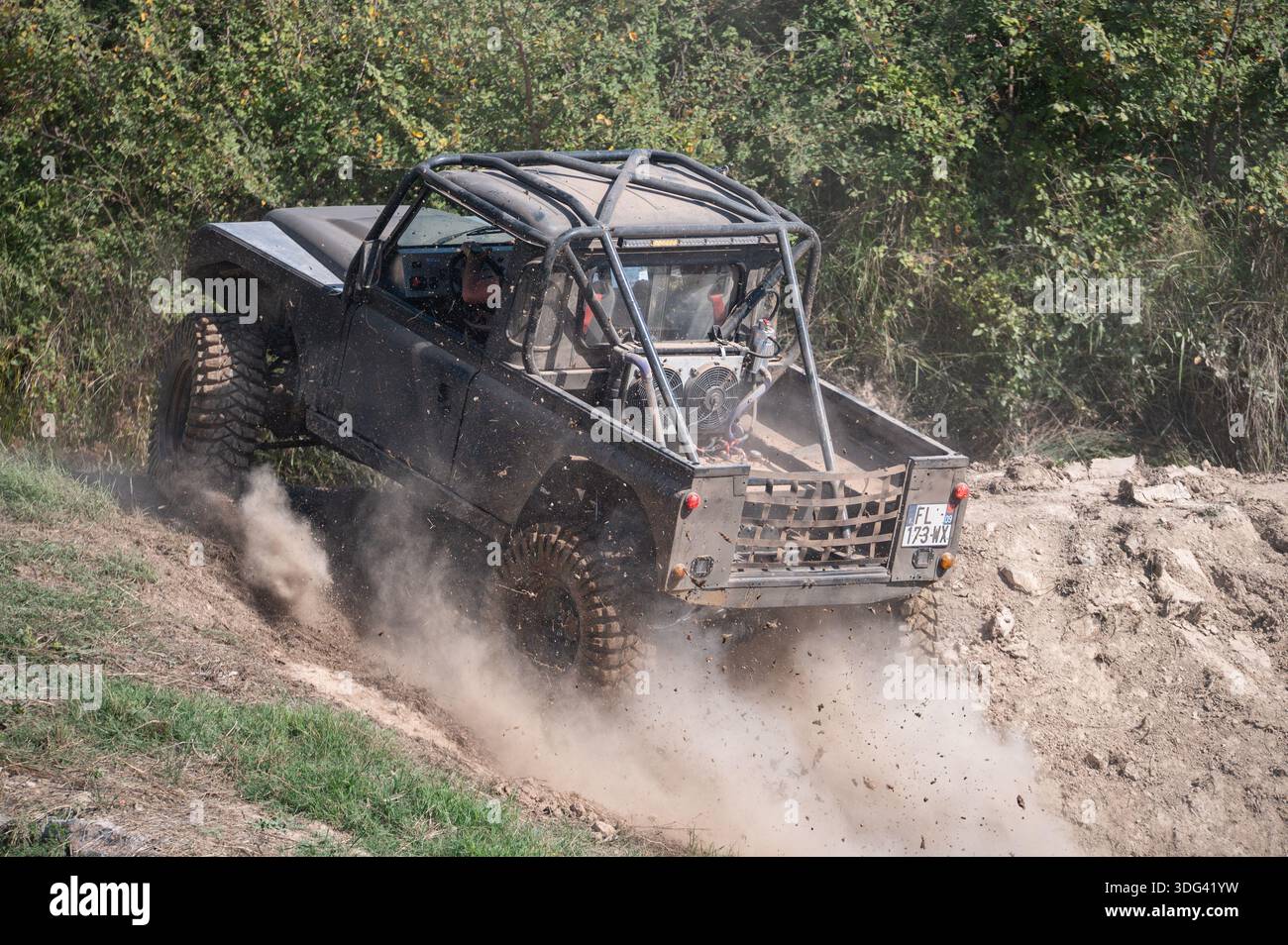 Rear view of a black modified Land Rover Defender pickup climbing a ...