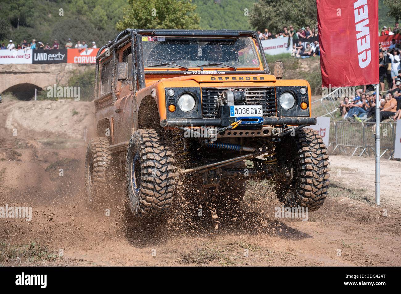 Front view of an orange modified Land Rover Defender jumping over mud ...