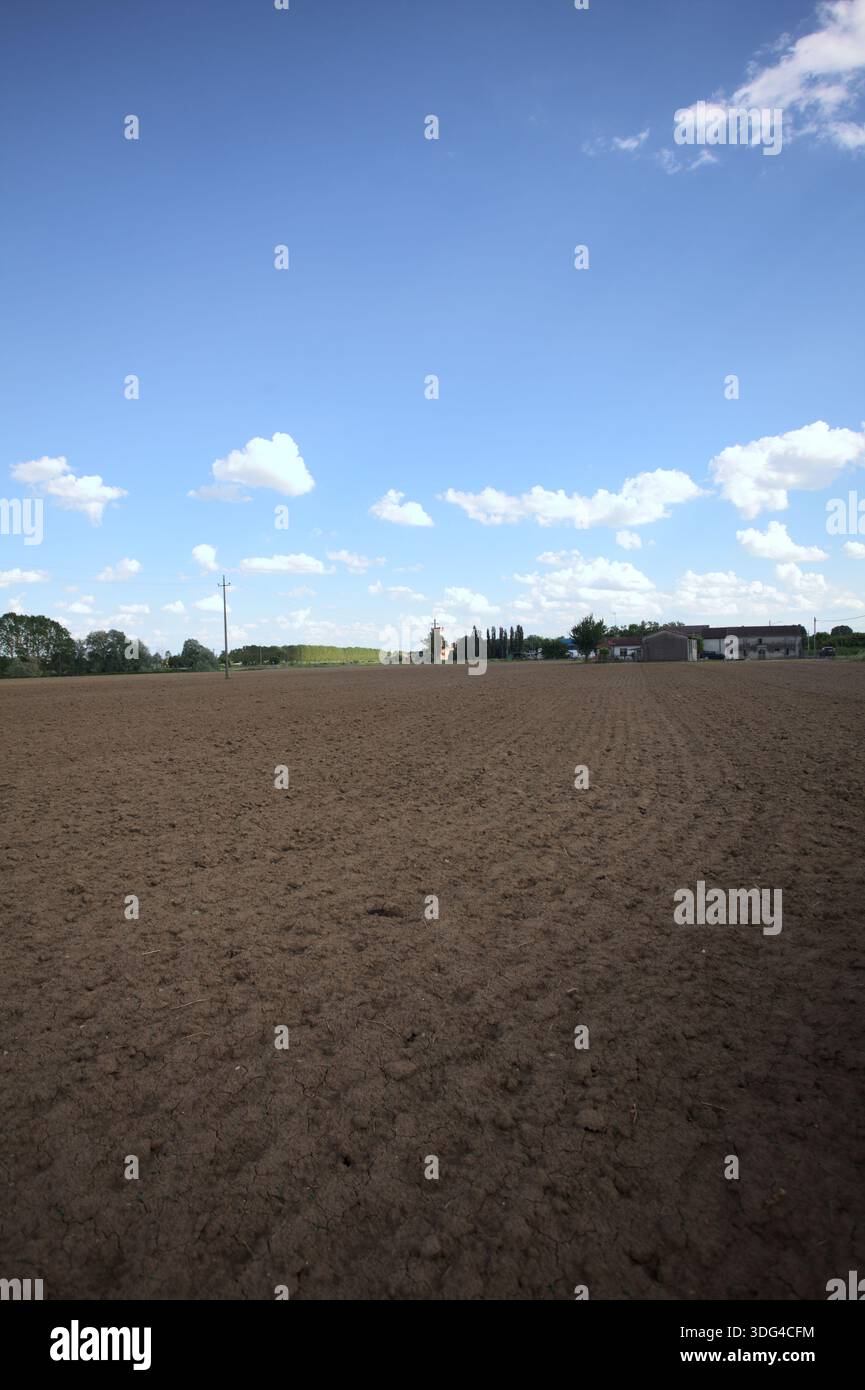 Ploughed field with trees and buildings of a village in the background ...